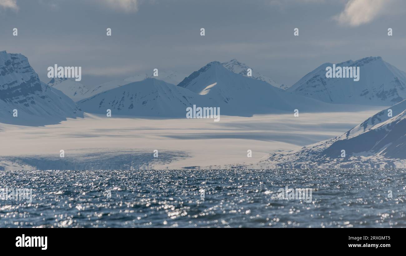 Snow covered mountains and a glacier by an arctic fjord with waves ...