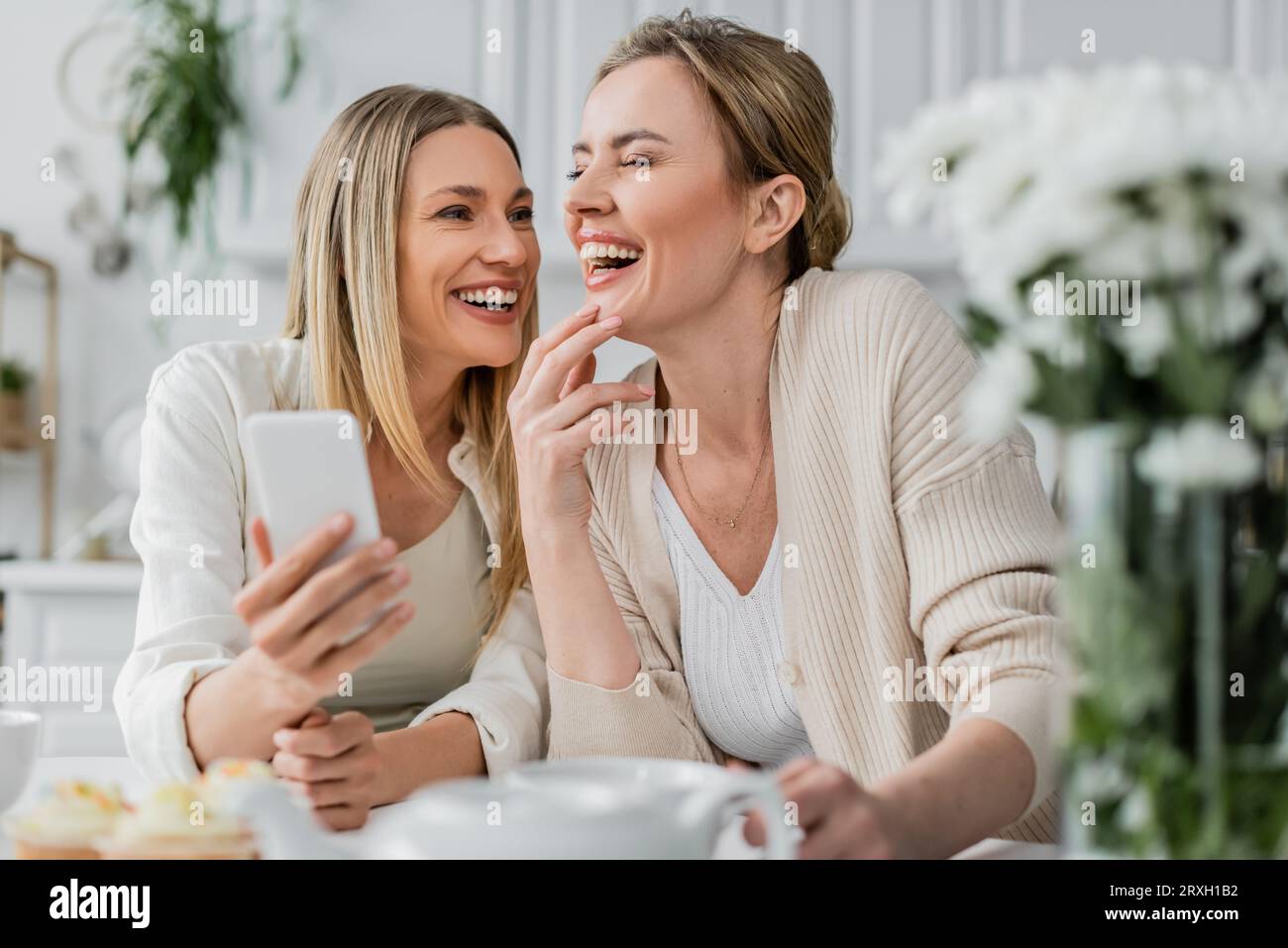 two attractive sisters in pastel cardigans laughing and holding mobile ...