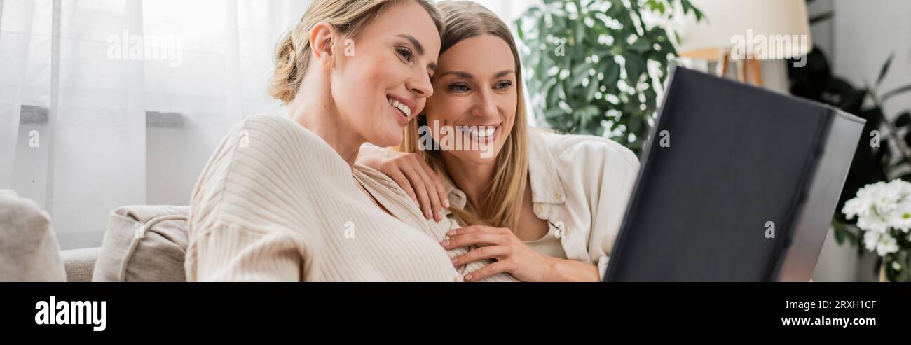 young blonde sisters hugging and looking at photo album on white ...