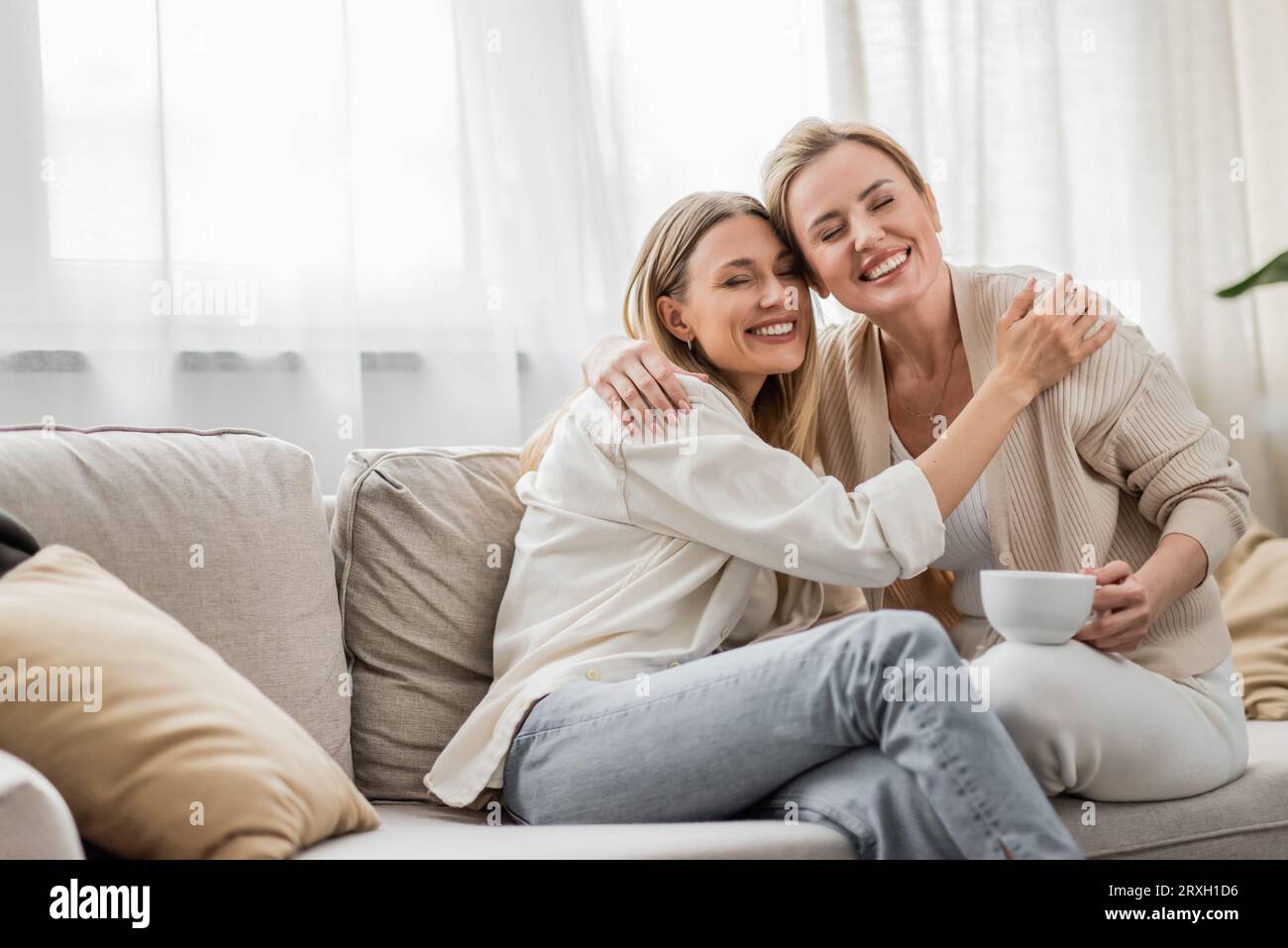 two good looking blonde sisters sitting on sofa and hugging with closed ...