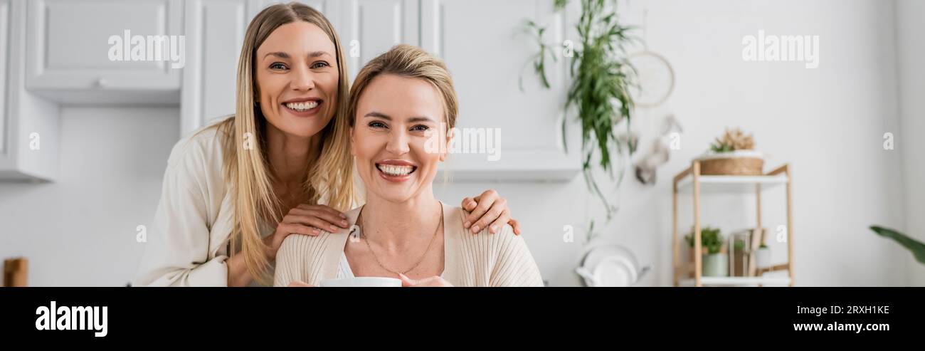 blonde sisters smiling and looking at camera on kitchen backdrop with ...
