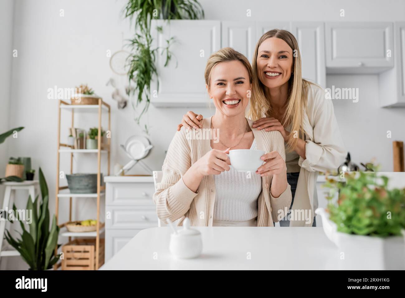 two blonde sisters drinking tea and smiling on kitchen background with ...