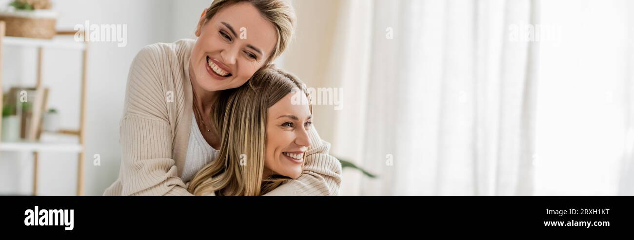 pretty sisters in trendy attire hugging and smiling sincerely on ...