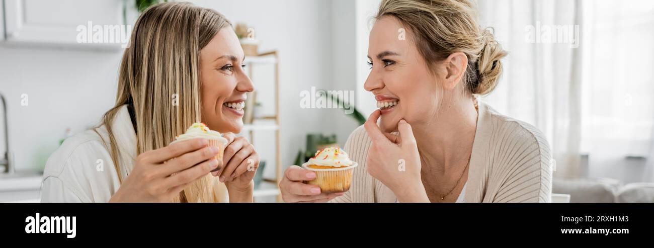 attractive classy sisters in pastel outfit enjoying cupcakes on kitchen ...