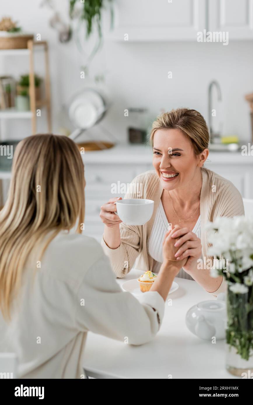 classy smiley blonde sisters in pastel cardigans holding hands and ...
