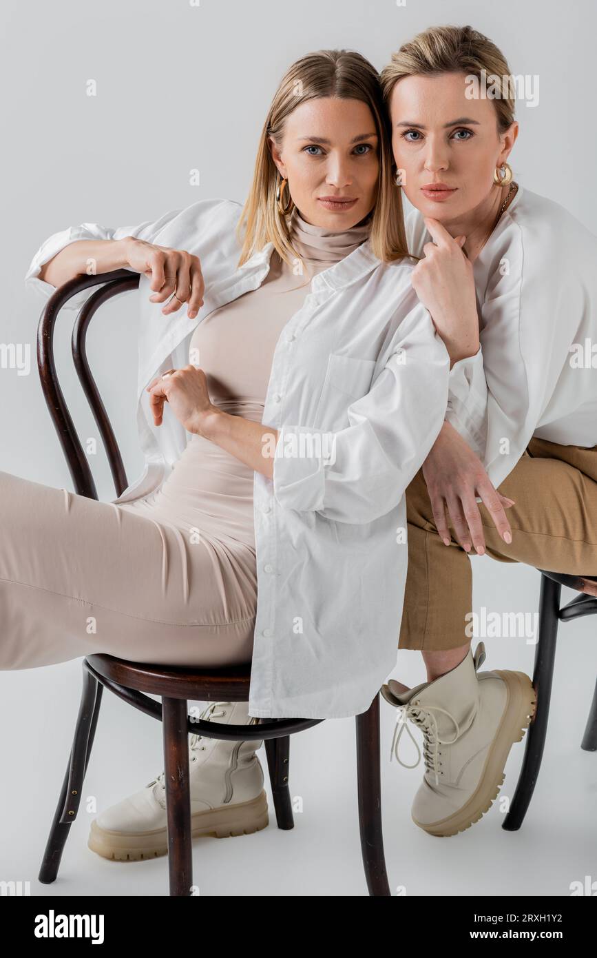 stylish elegant blonde sisters sitting on chairs in fashionable pastel ...
