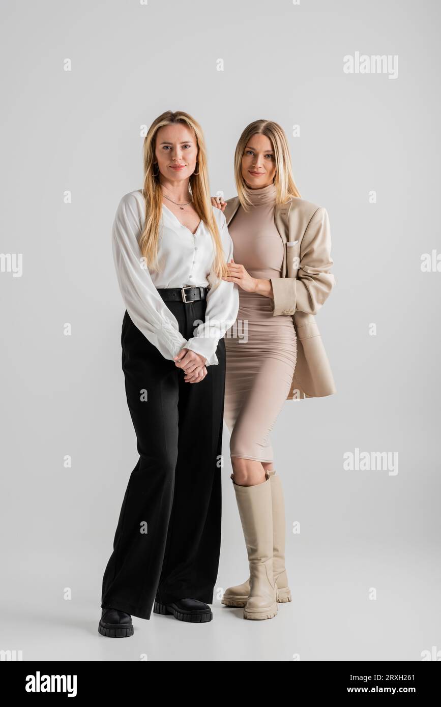 attractive stylish sisters in formal outfit posing on grey background, bonding, fashion concept ...