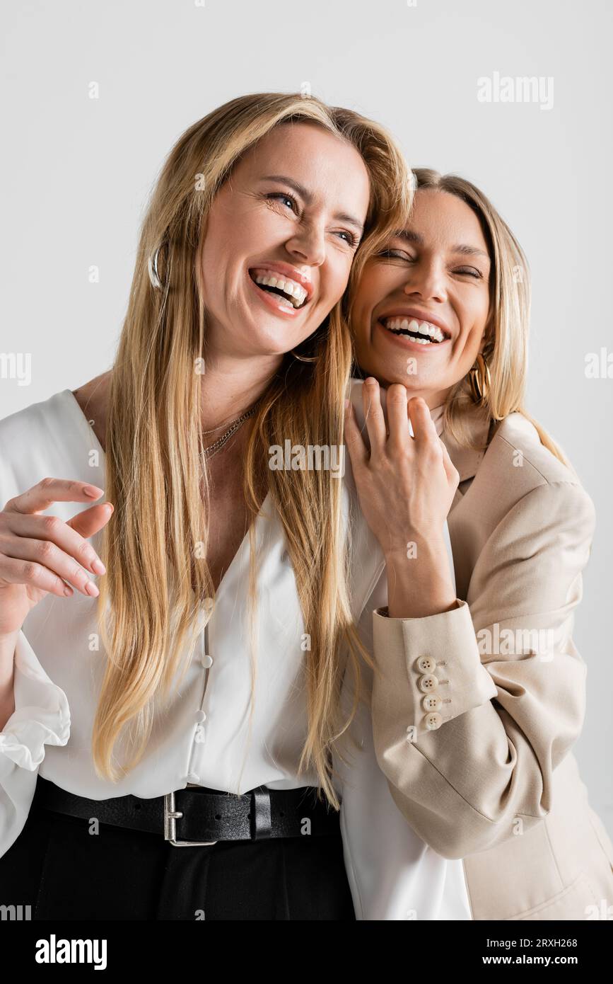 portrait of two elegant attractive sisters laughing posing on grey backdrop, bonding, fashion ...