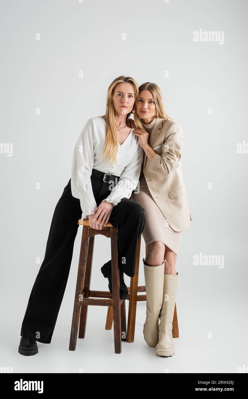 two fashionable stylish sisters in formal outfits sitting on chairs ...