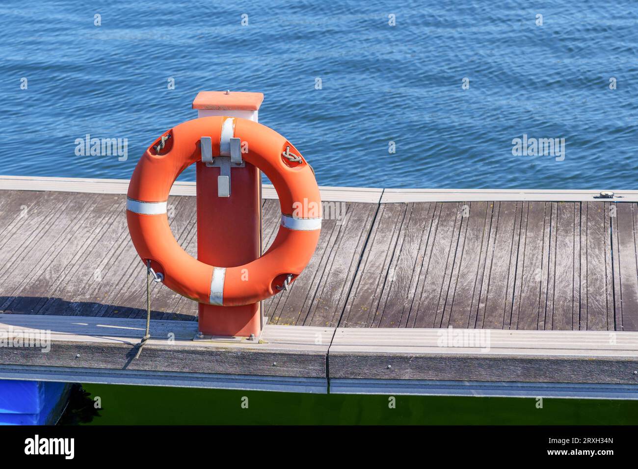 Orange lifebuoy hanging on post at sea boat dock with tranquil waves ...