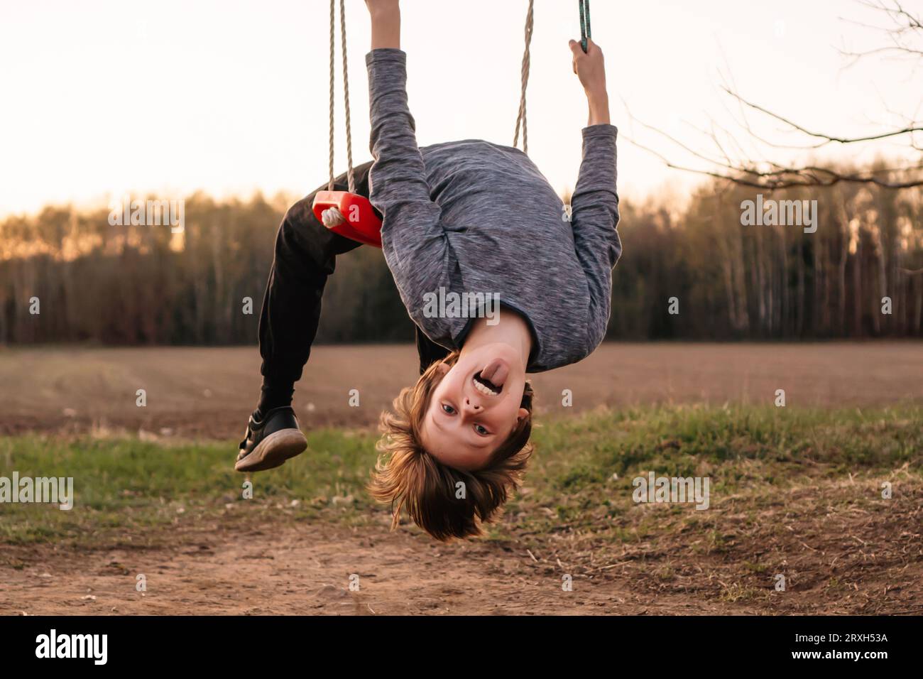 Delightful boy, wearing gray longsleeve, sitting on swings, tightly ...