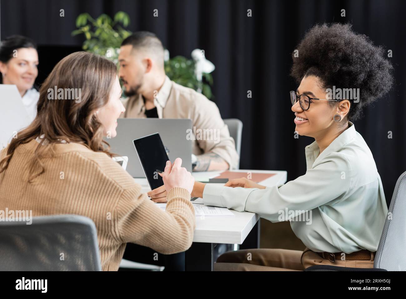 happy interracial female colleagues talking in modern coworking ...