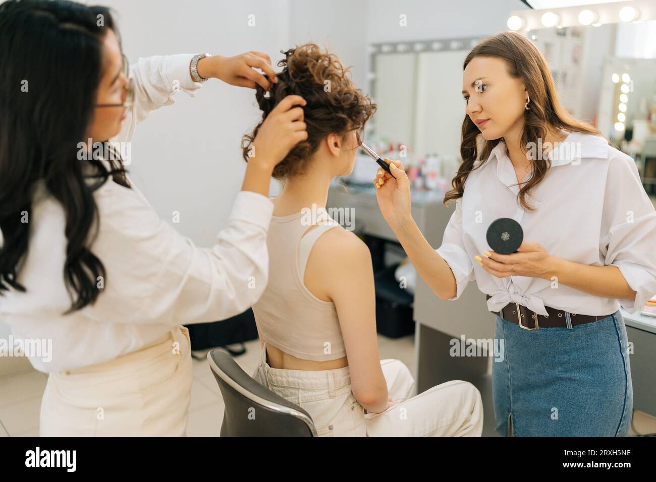 Rear view of elegance curly young woman getting professional makeup ...