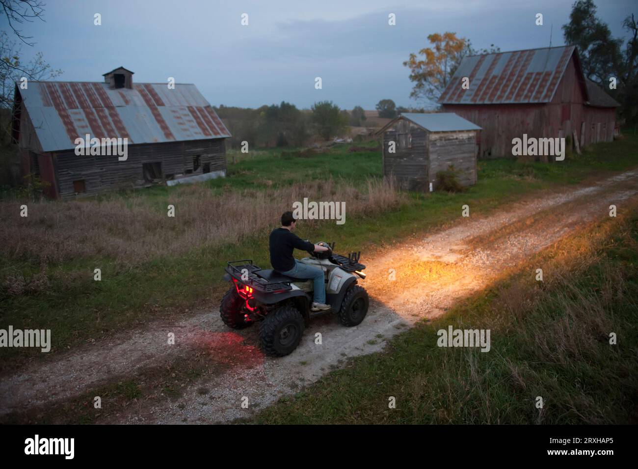 Teenage boy drives a 4-wheeler down a gravel road on a farm; Dunbar ...