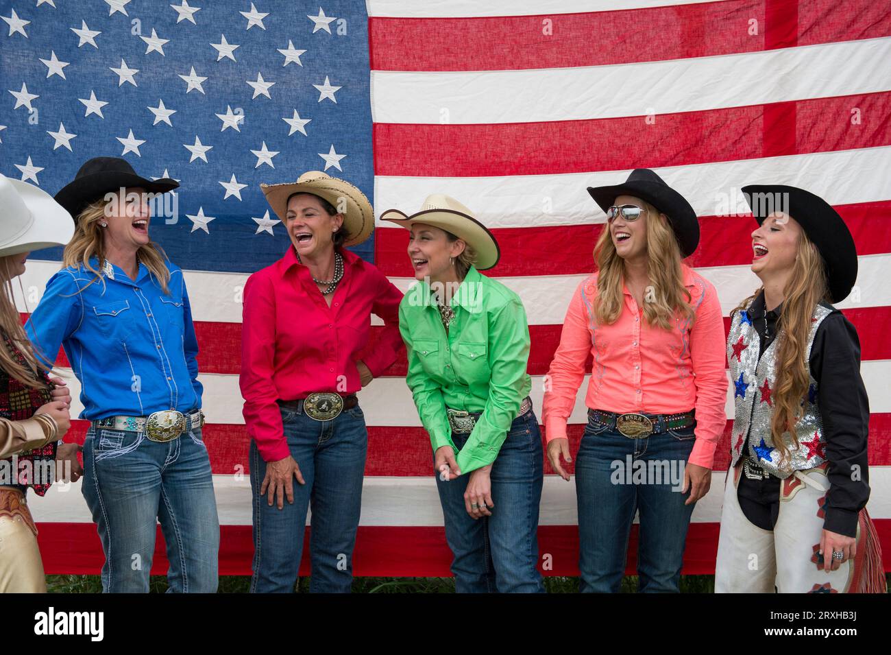 Rodeo queens laugh during a photo shoot in front of an American flag ...
