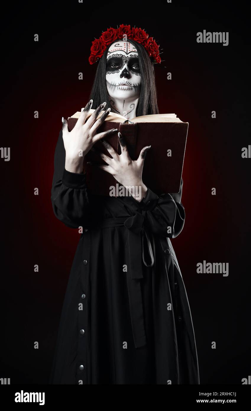 Young woman with calavera (sugar skull) makeup holds book (grimoire) in ...