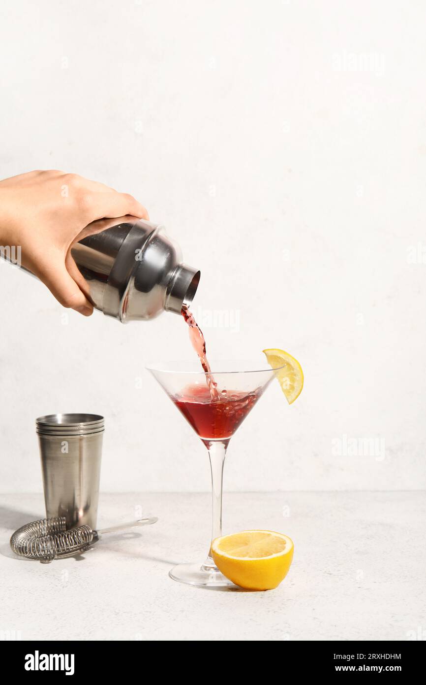 Woman pouring Cosmopolitan cocktail from shaker into glass on white ...