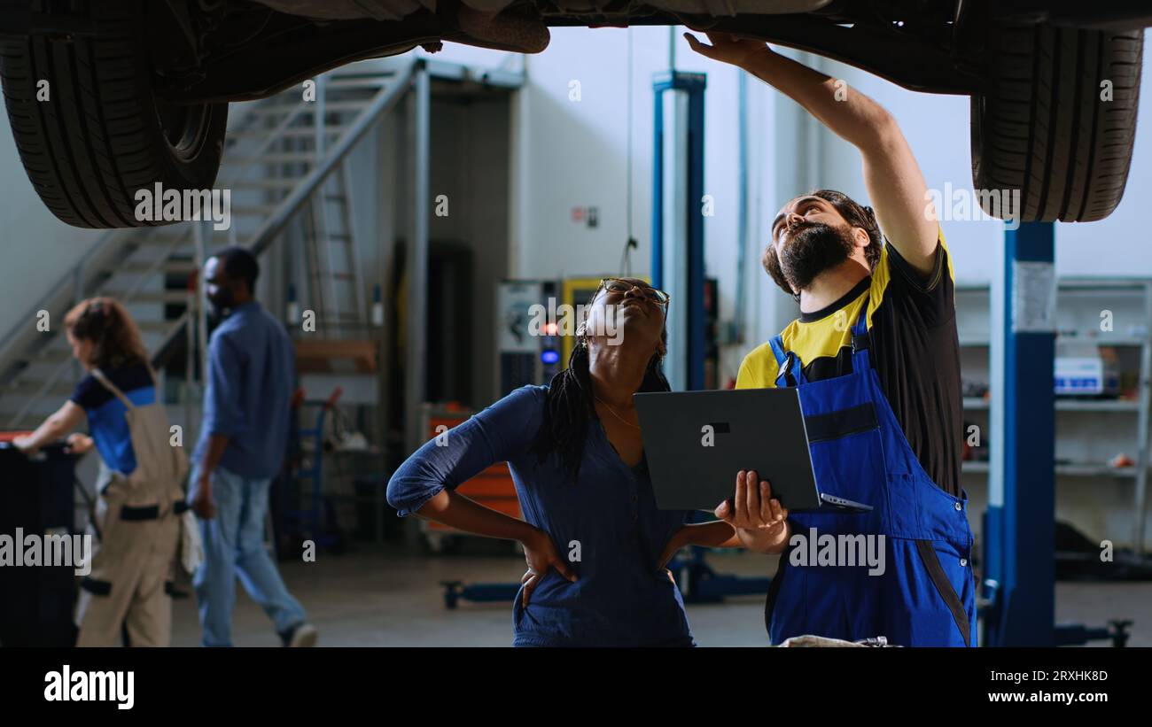 Mechanic in garage workspace standing with customer underneath ...