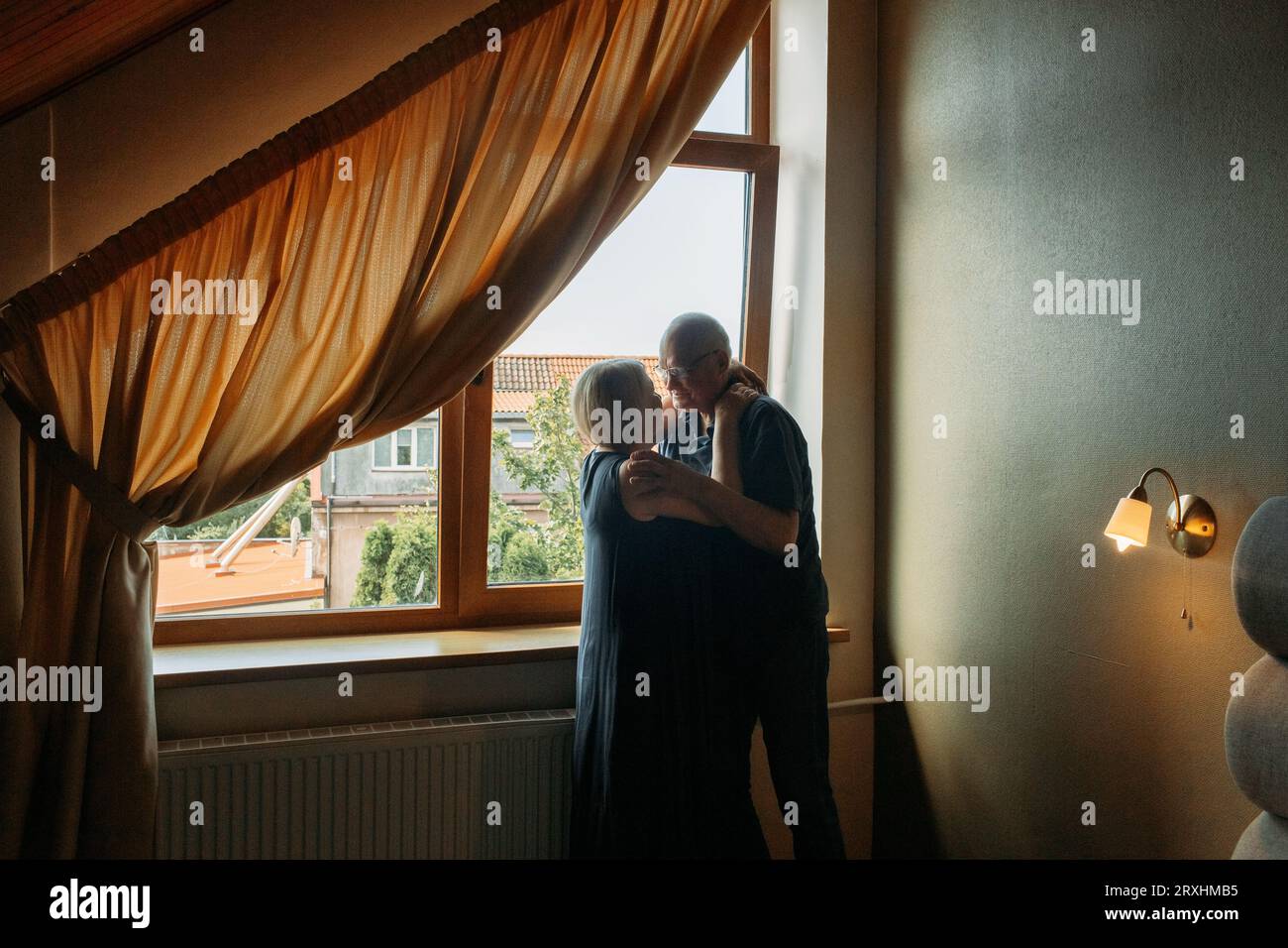 A happy elderly couple are standing near the window, hugging Stock ...