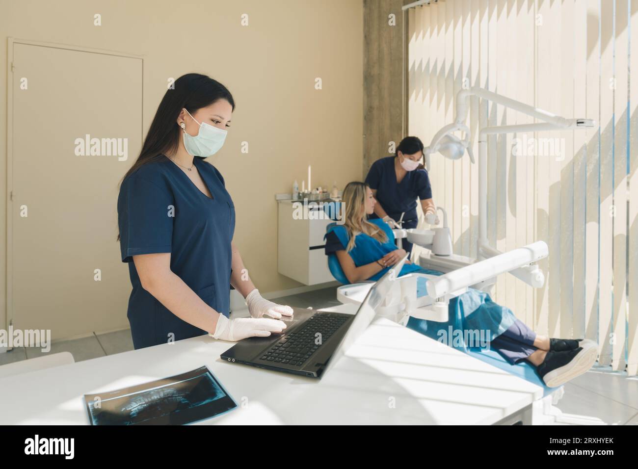 Female dentist typing patient data on laptop computer while patient ...