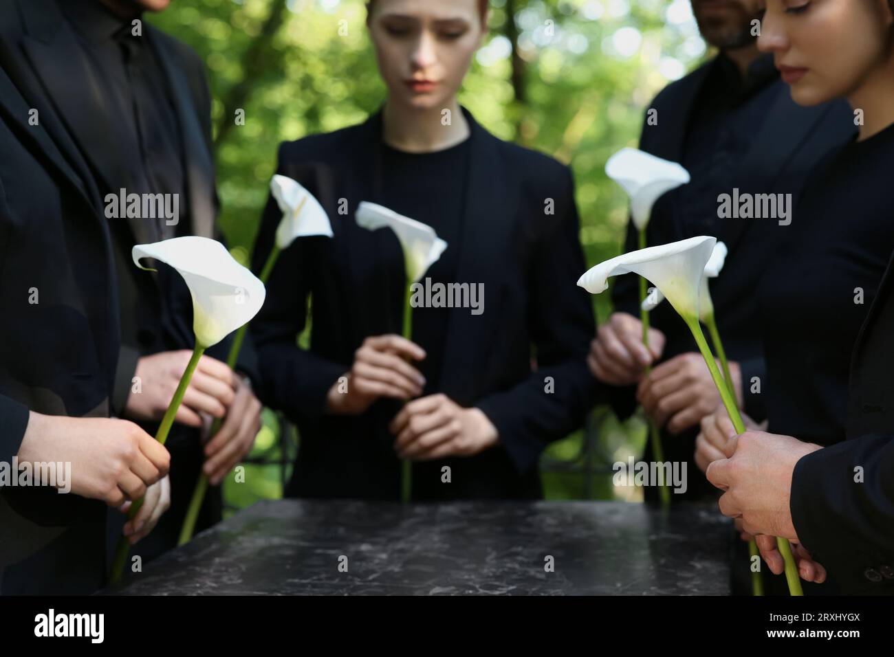People with calla lily flowers near granite tombstone at cemetery ...