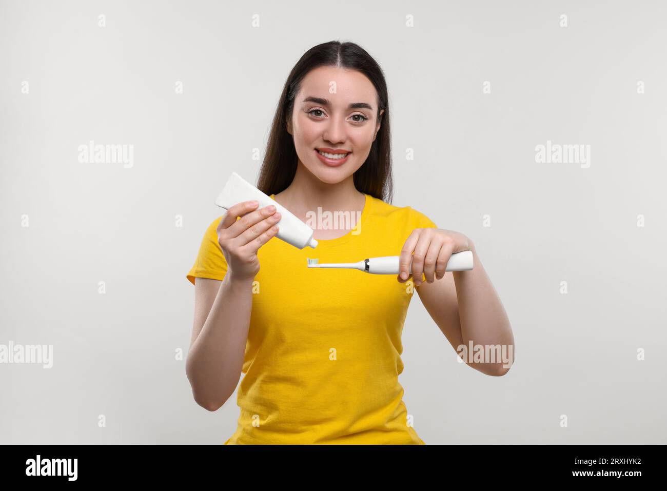 Happy young woman squeezing toothpaste from tube onto electric ...
