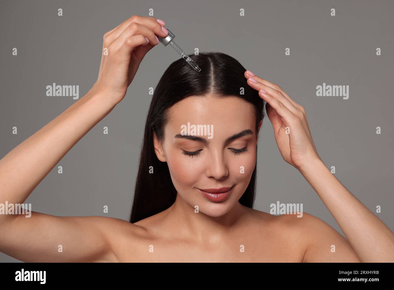 Beautiful woman applying hair serum on grey background. Cosmetic ...