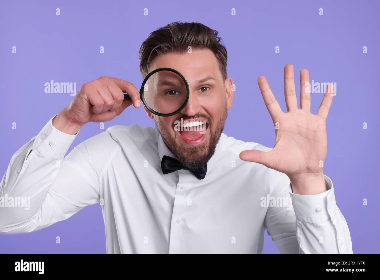 Emotional man looking through magnifier on violet background Stock ...