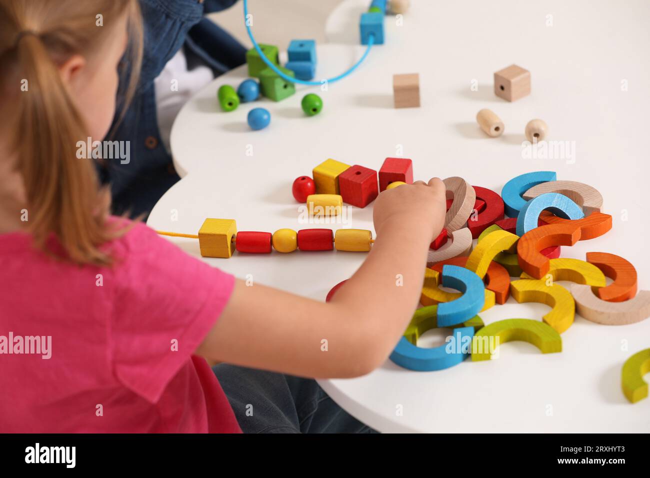 Little children playing with wooden pieces and string for threading ...