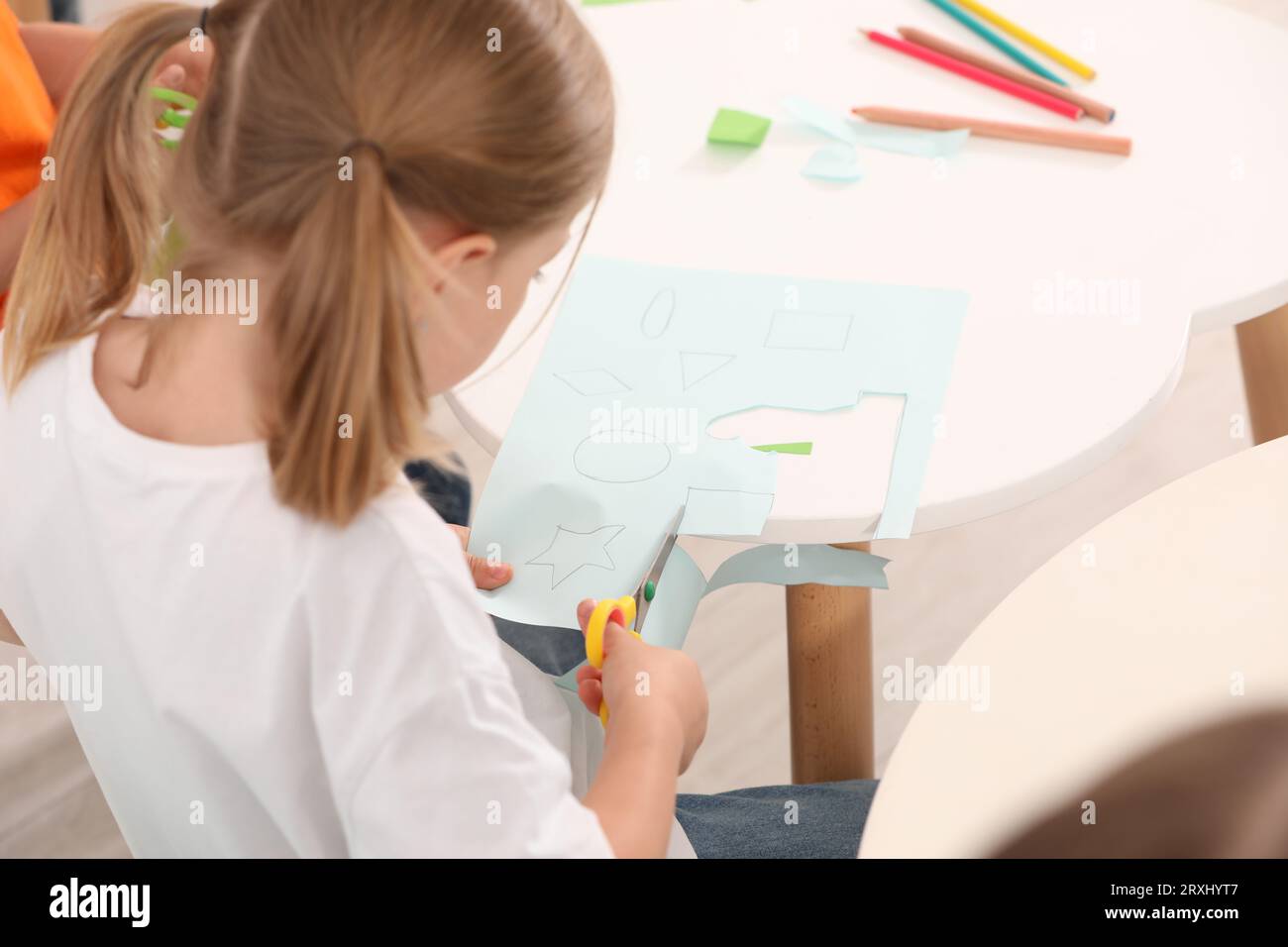 Little girl cutting color paper with scissors at desk, closeup ...