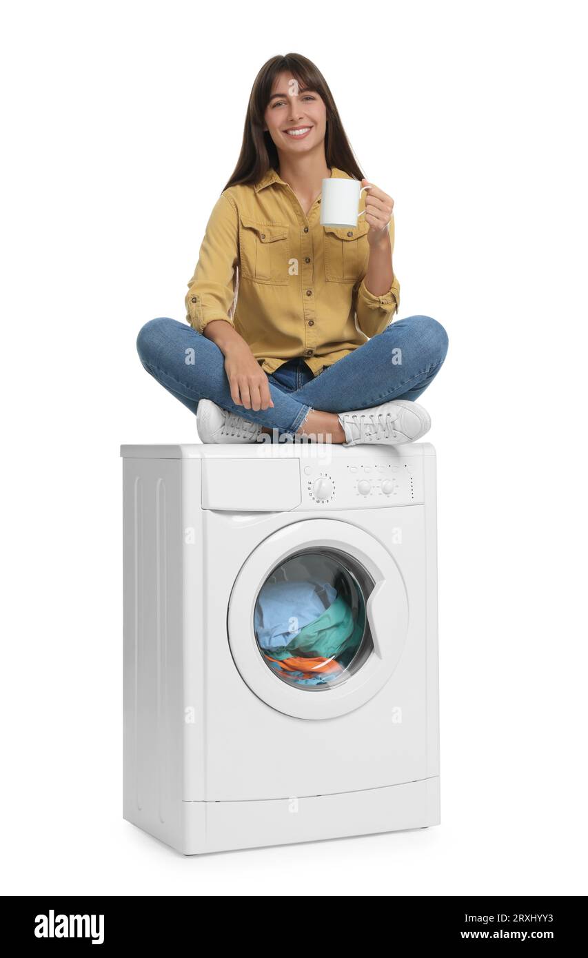 Beautiful woman with cup of drink sitting on washing machine against ...