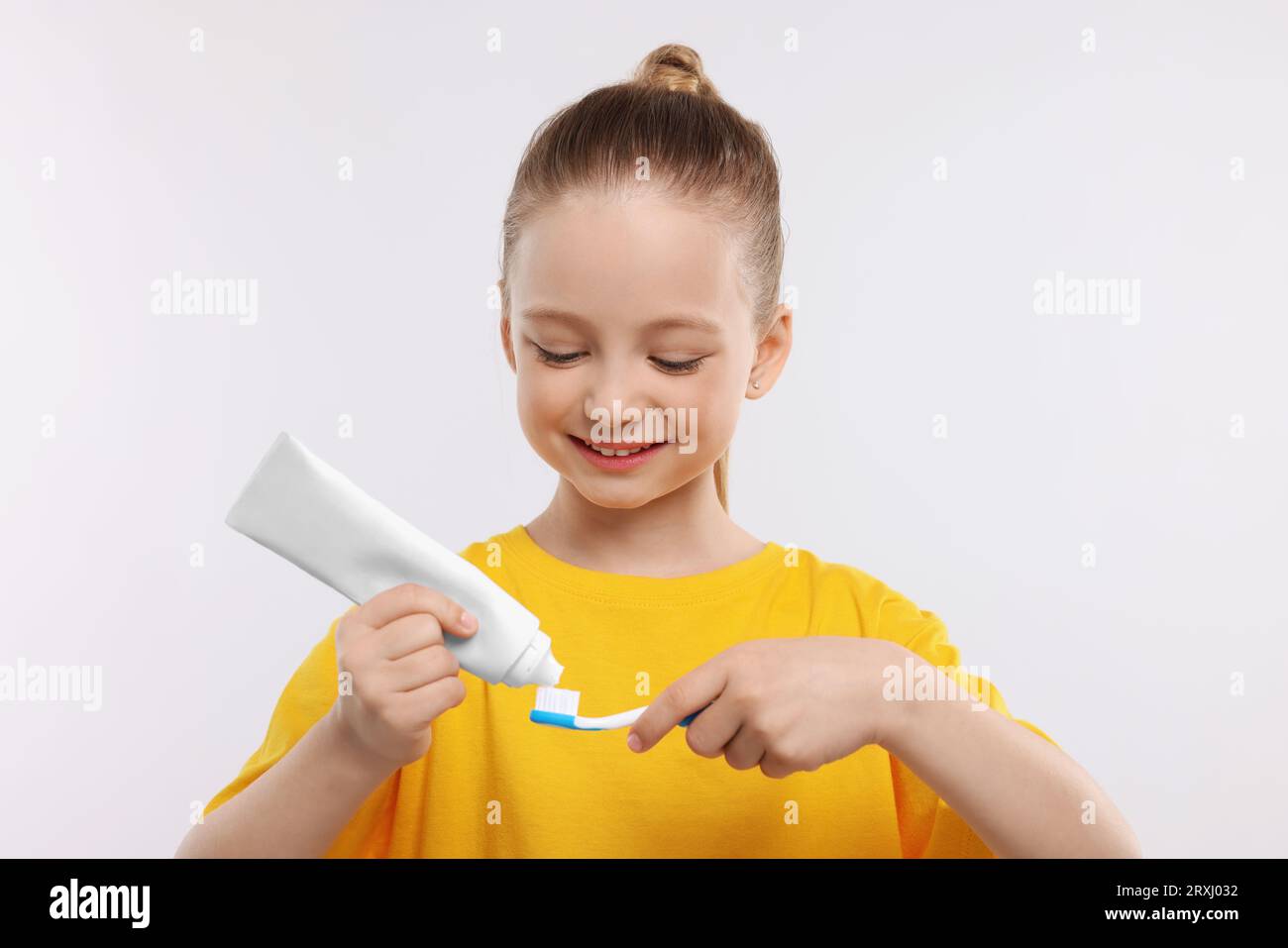 Happy girl squeezing toothpaste from tube onto toothbrush on white ...