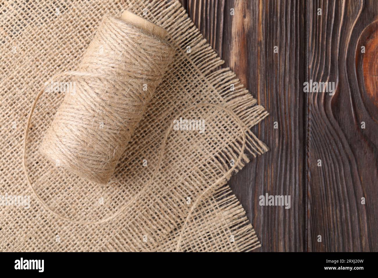 Spool of thread and burlap fabric on wooden table, top view. Space for ...