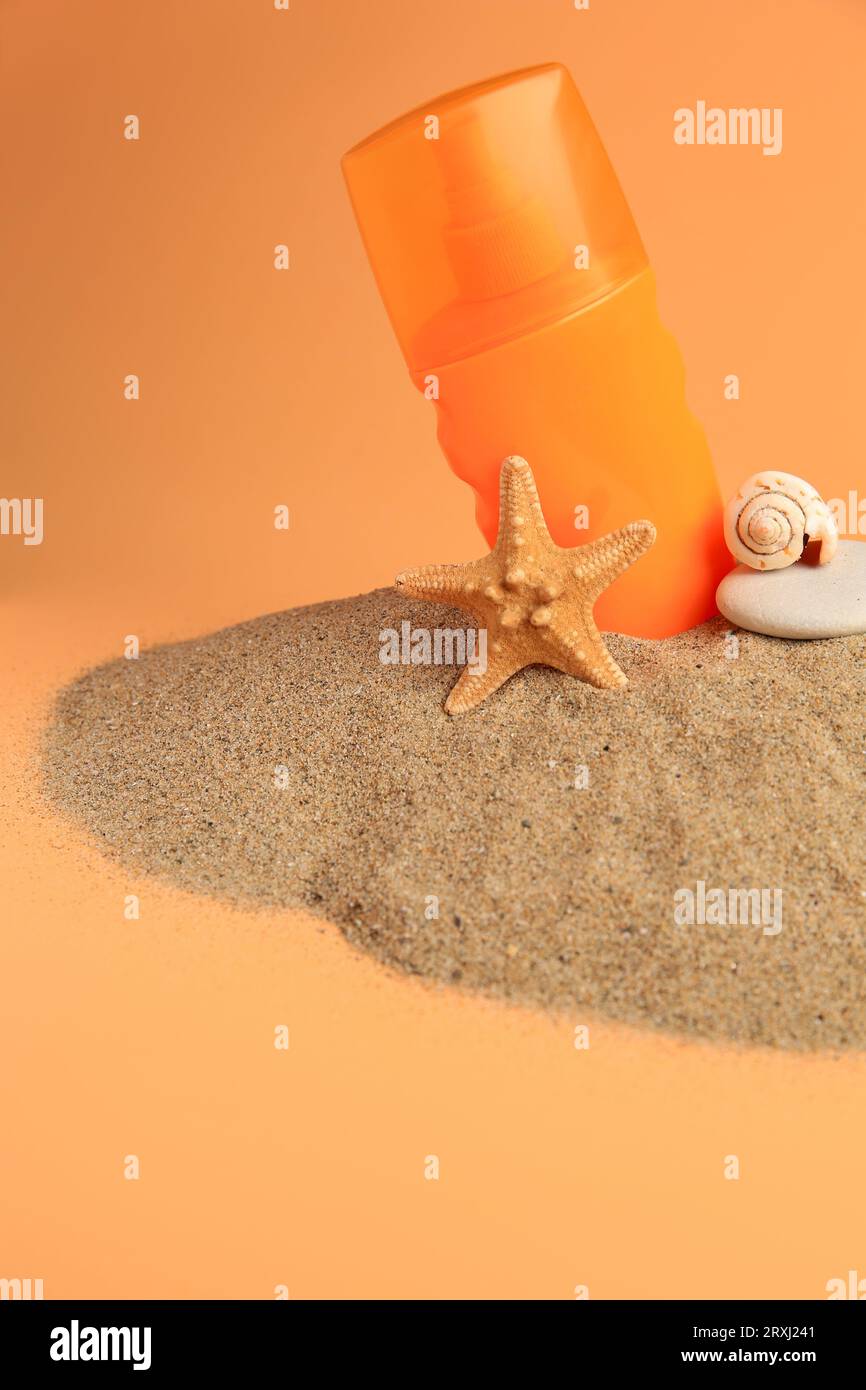 Sand with bottle of sunscreen, starfish, stone and seashell against ...