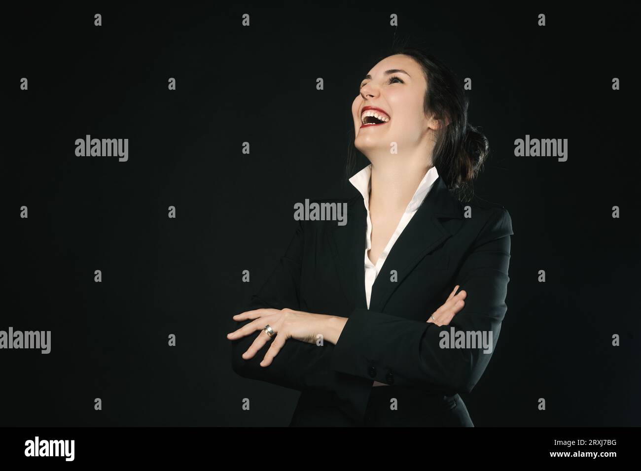 Woman with tied-back hair, in black business dress, laughing against a ...