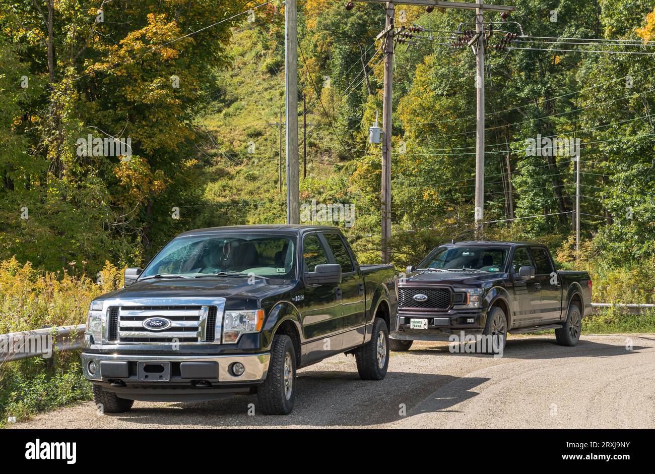 Two Ford four door pickup trucks parked on the side of the road in ...