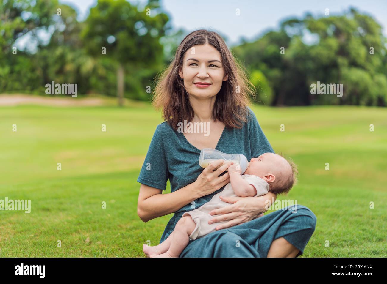 Mother holding and feeding baby from milk bottle in the park. Portrait ...
