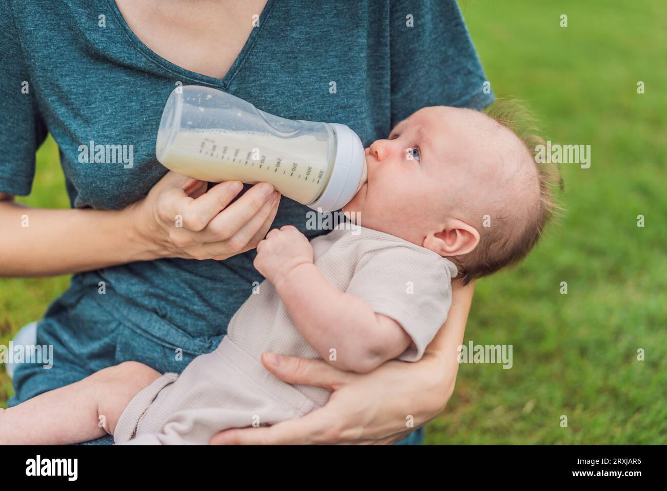 Mother holding and feeding baby from milk bottle in the park. Portrait ...