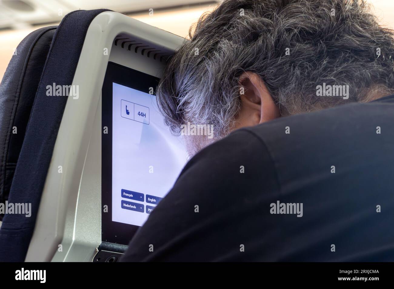 A passenger in an airplane rests with his head resting on the display ...