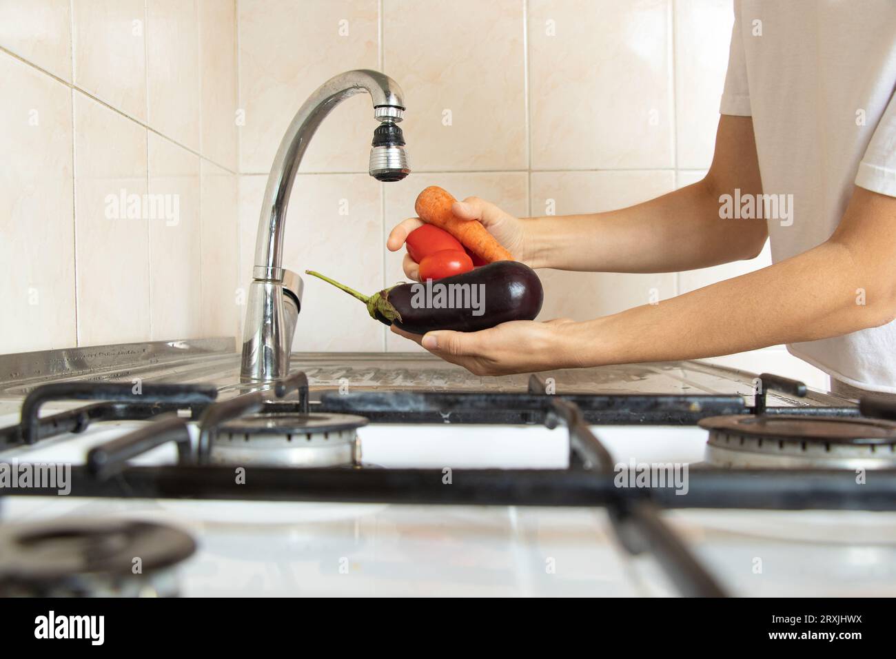 A girl washes eggplant and tomatoes and carrots under the kitchen ...