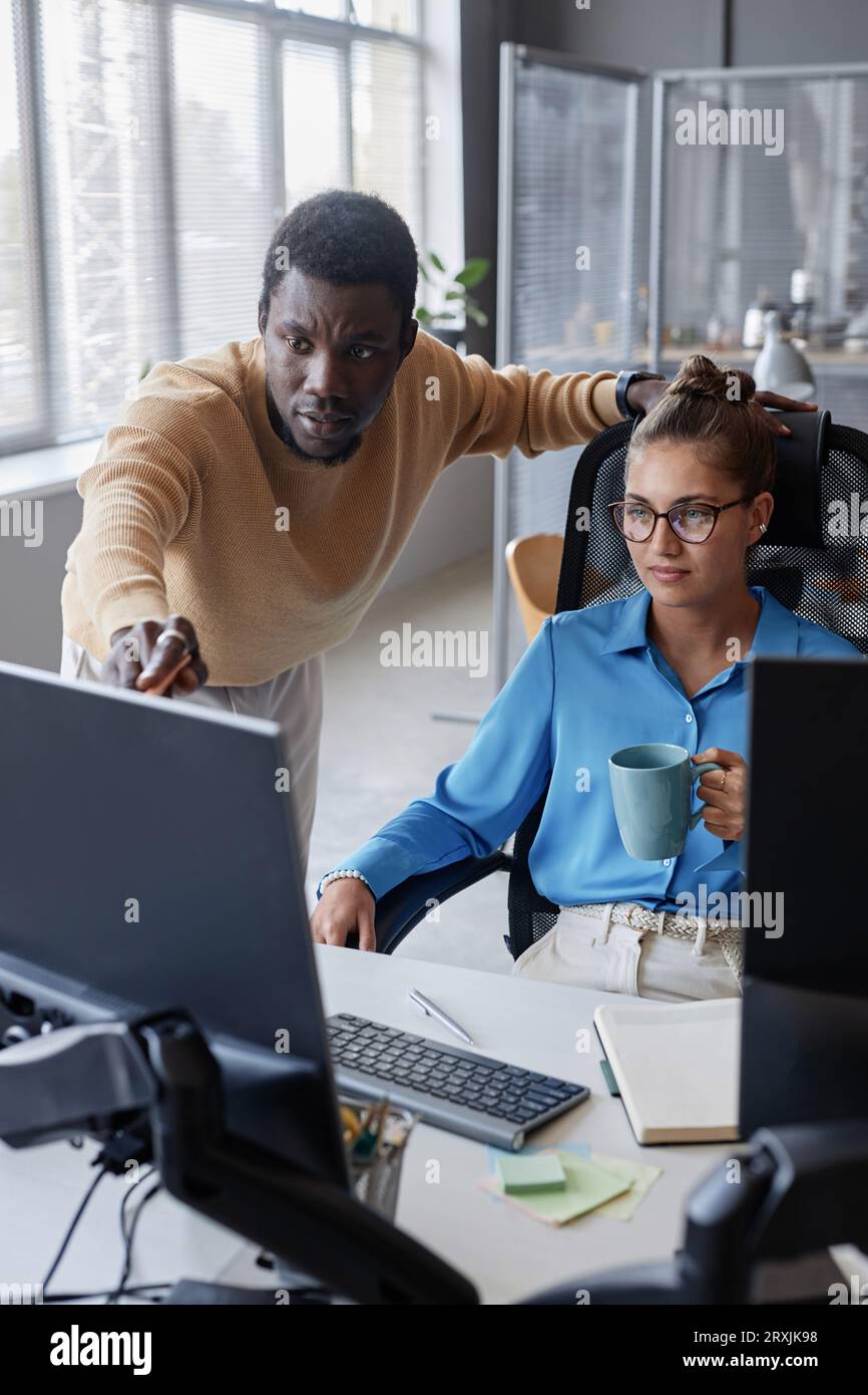 Vertical image of young colleagues discussing presentation on computer ...