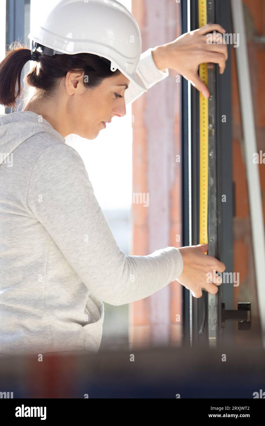 young female construction worker measuring the wall with measuring tape ...