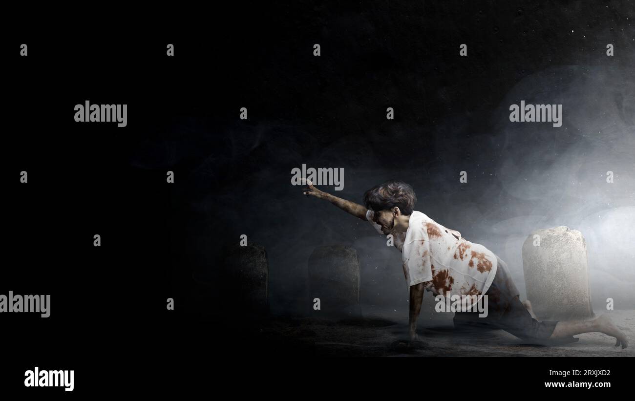 A scary zombie with blood and wounds on his body crawls in the cemetery ...