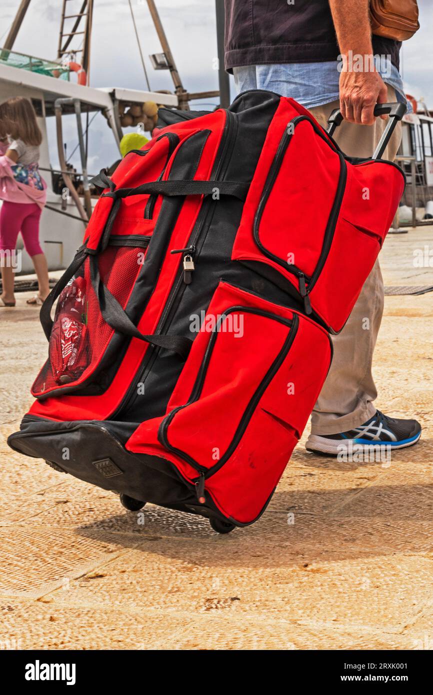 carry a huge red suitcase, a bag on wheels, to the pier to the ship ...