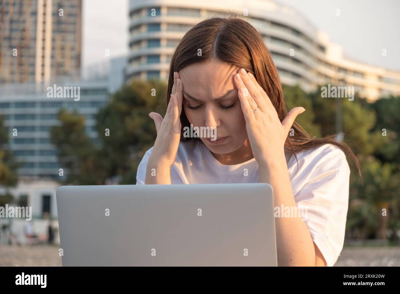 Stressed woman freelancer working on laptop outdoor with headache ...