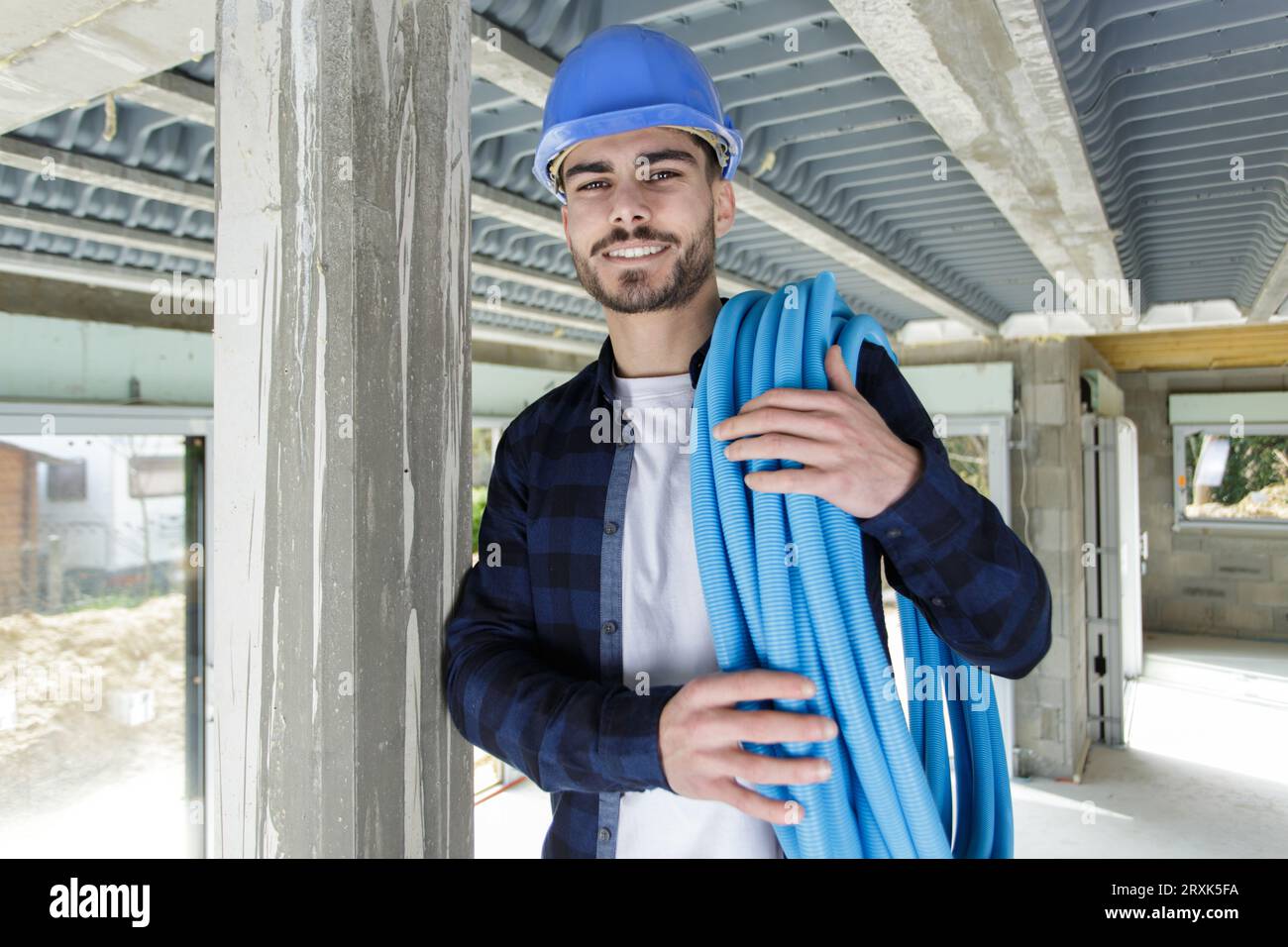 builder with reel of blue pipe over his shoulder Stock Photo - Alamy