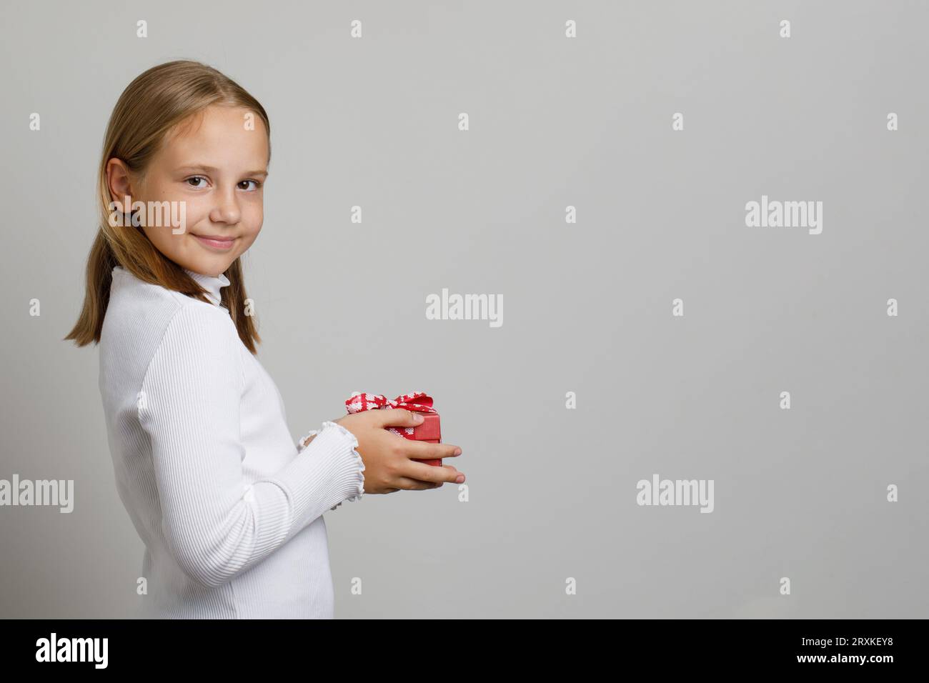 Happy smiling child girl with red gift present box on white studio wall ...