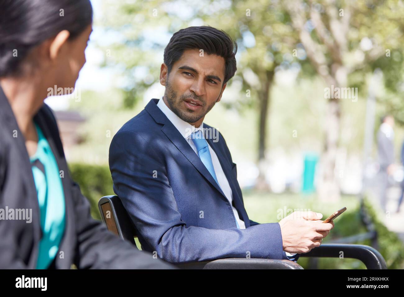 Businessman talking to his colleague on park bench Stock Photo - Alamy