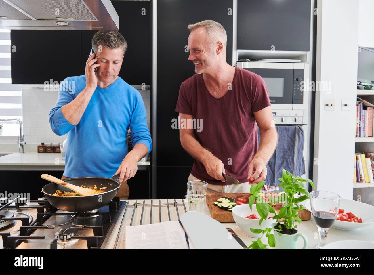 Man on phone while cooking with partner Stock Photo - Alamy