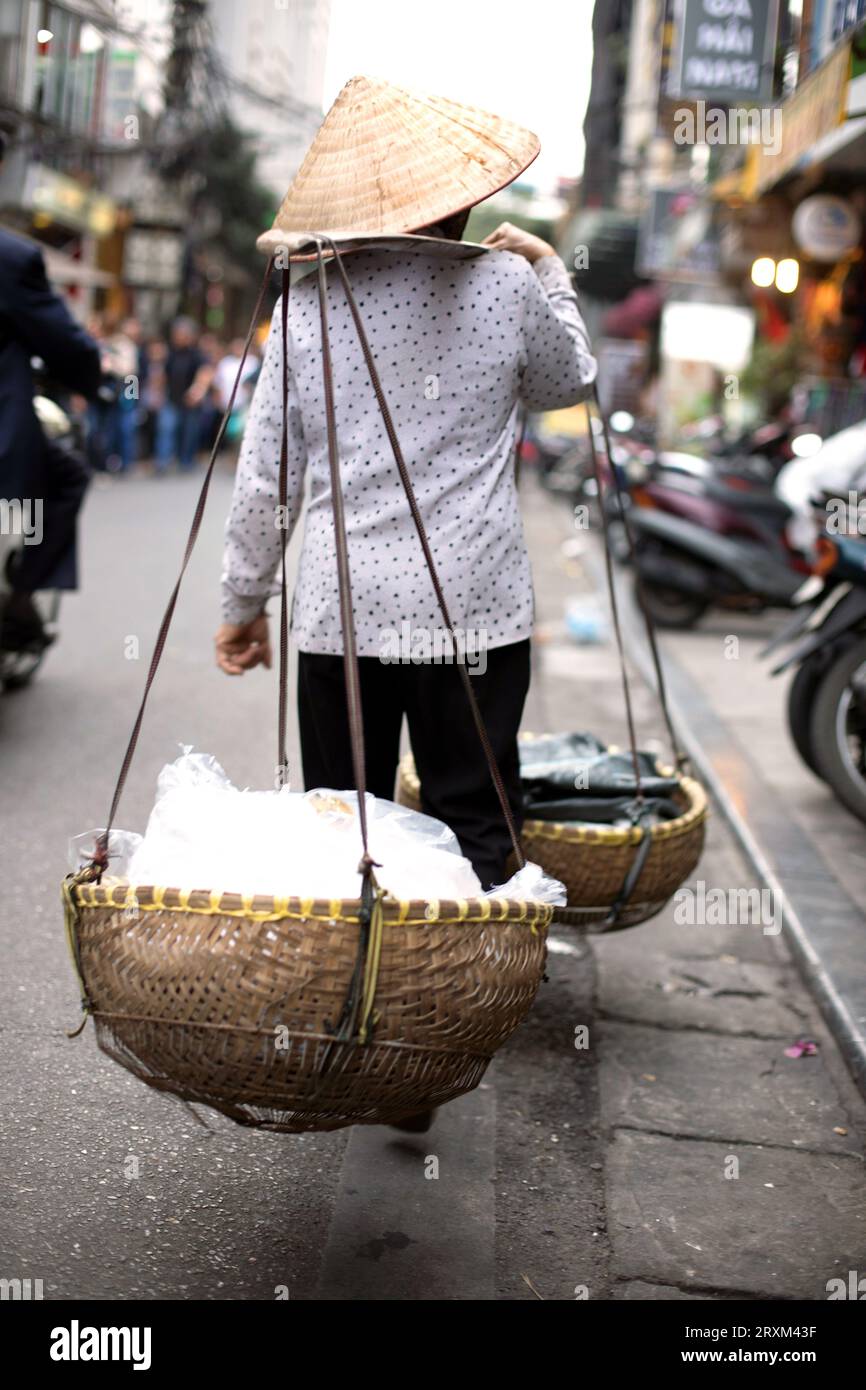 Woman in Asian conical hat walking with carrying pole Stock Photo - Alamy